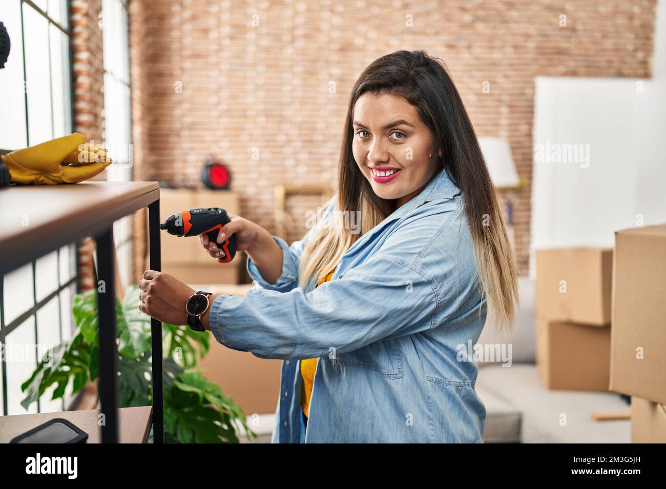 Young beautiful plus size woman smiling confident repairing shelving at ...