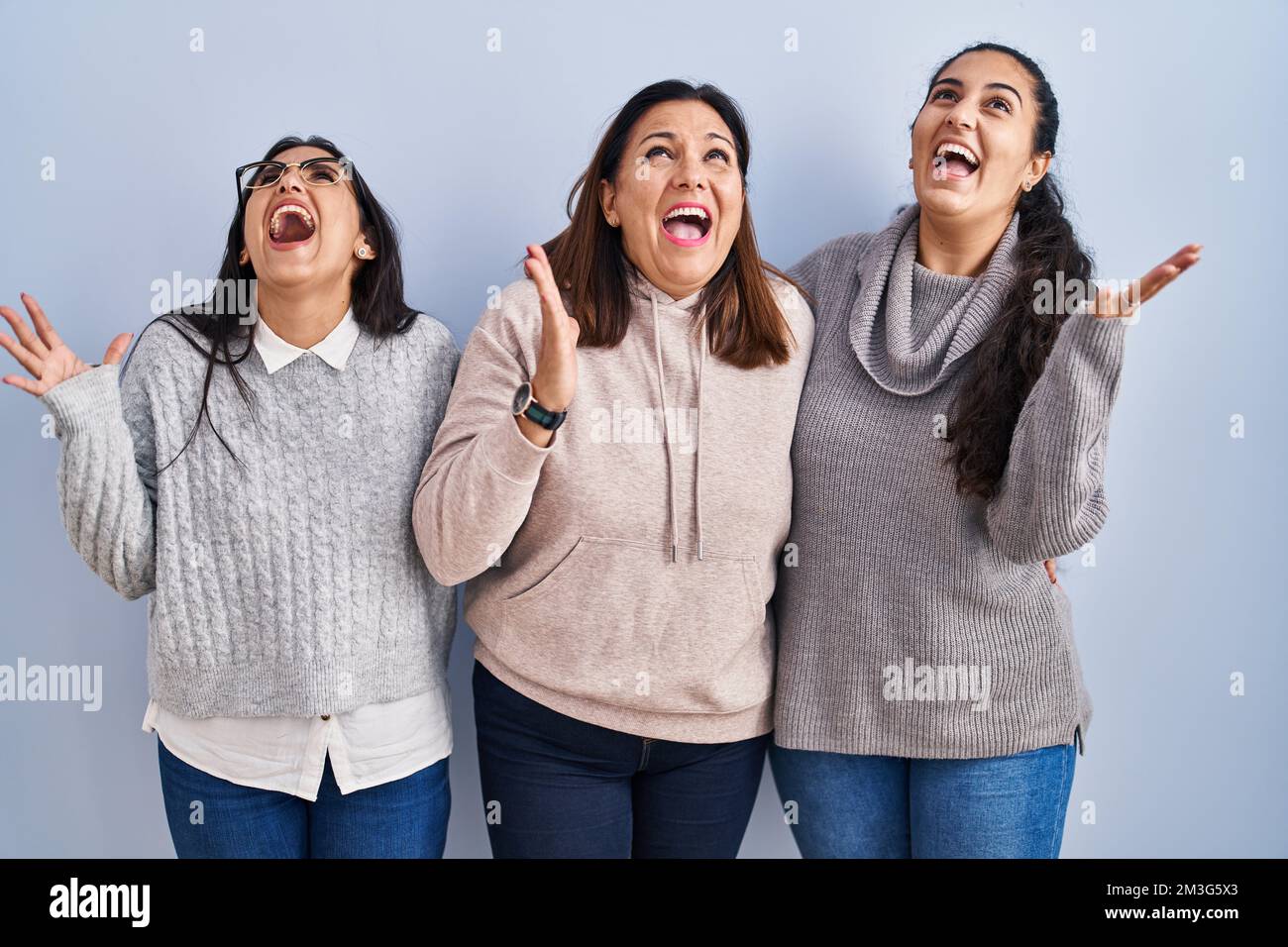 Mother and two daughters standing over blue background crazy and mad ...