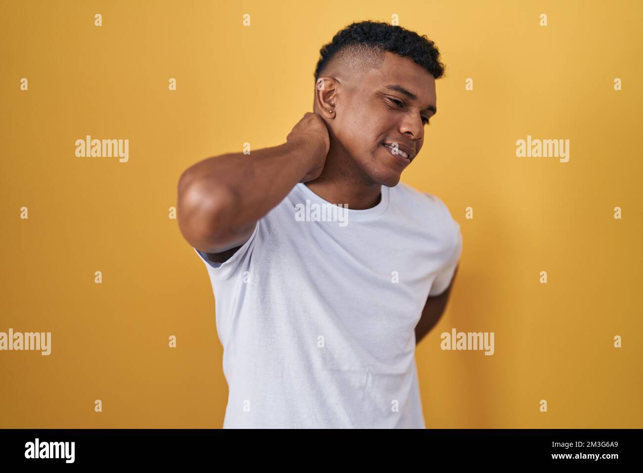 Young hispanic man standing over yellow background suffering of neck ...