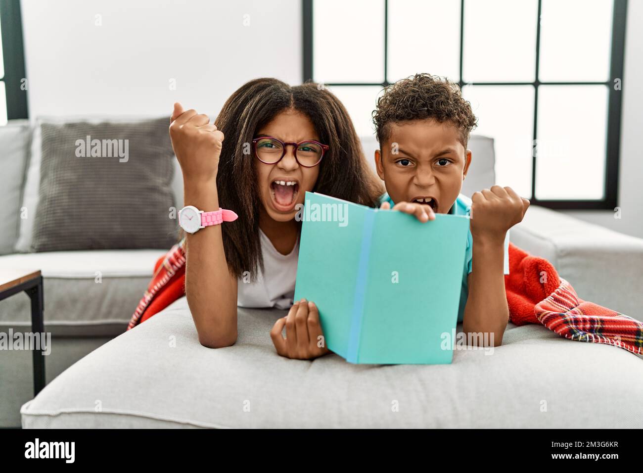 Two siblings lying on the sofa reading a book angry and mad raising ...