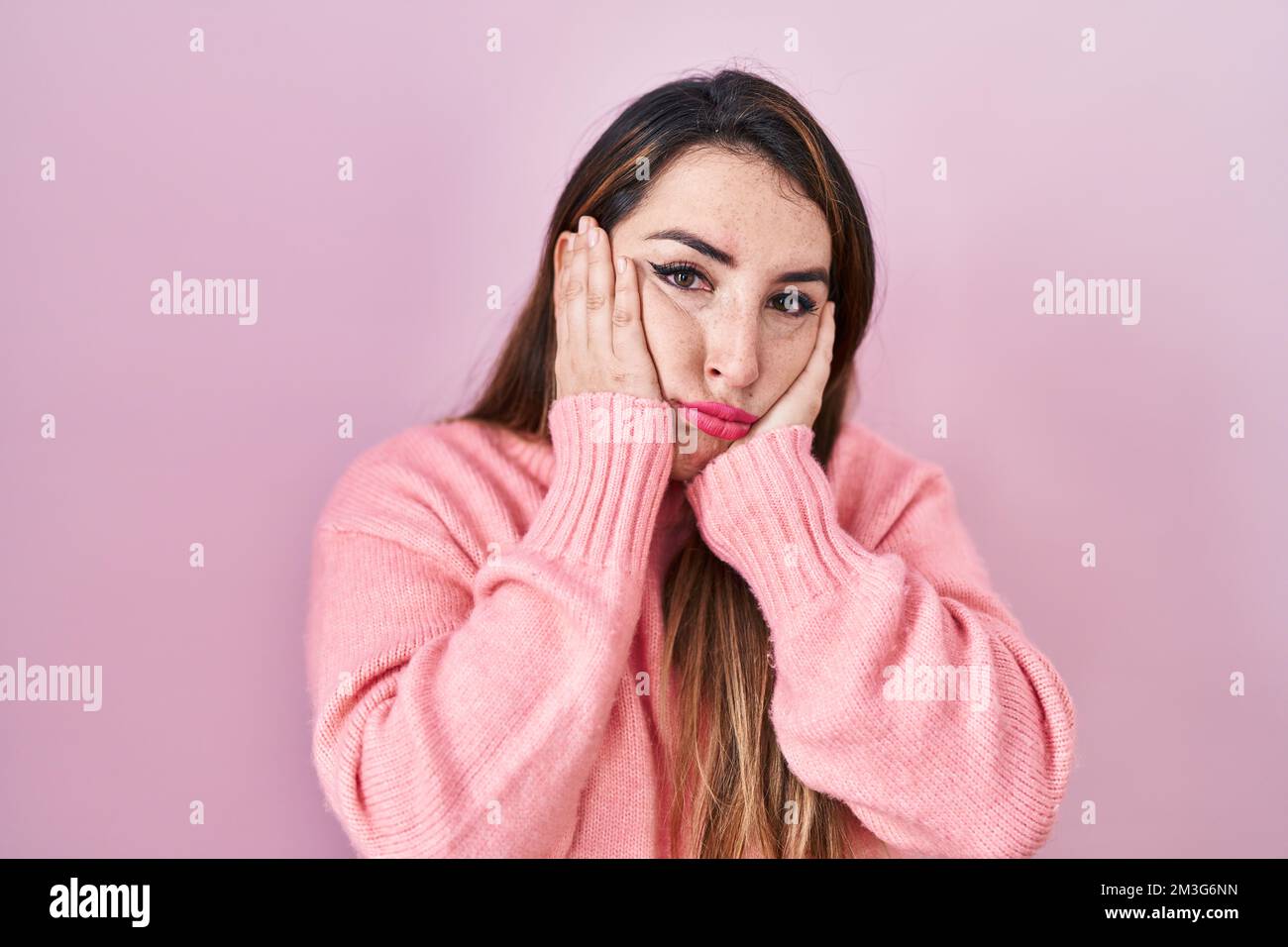 Young hispanic woman standing over pink background tired hands covering ...