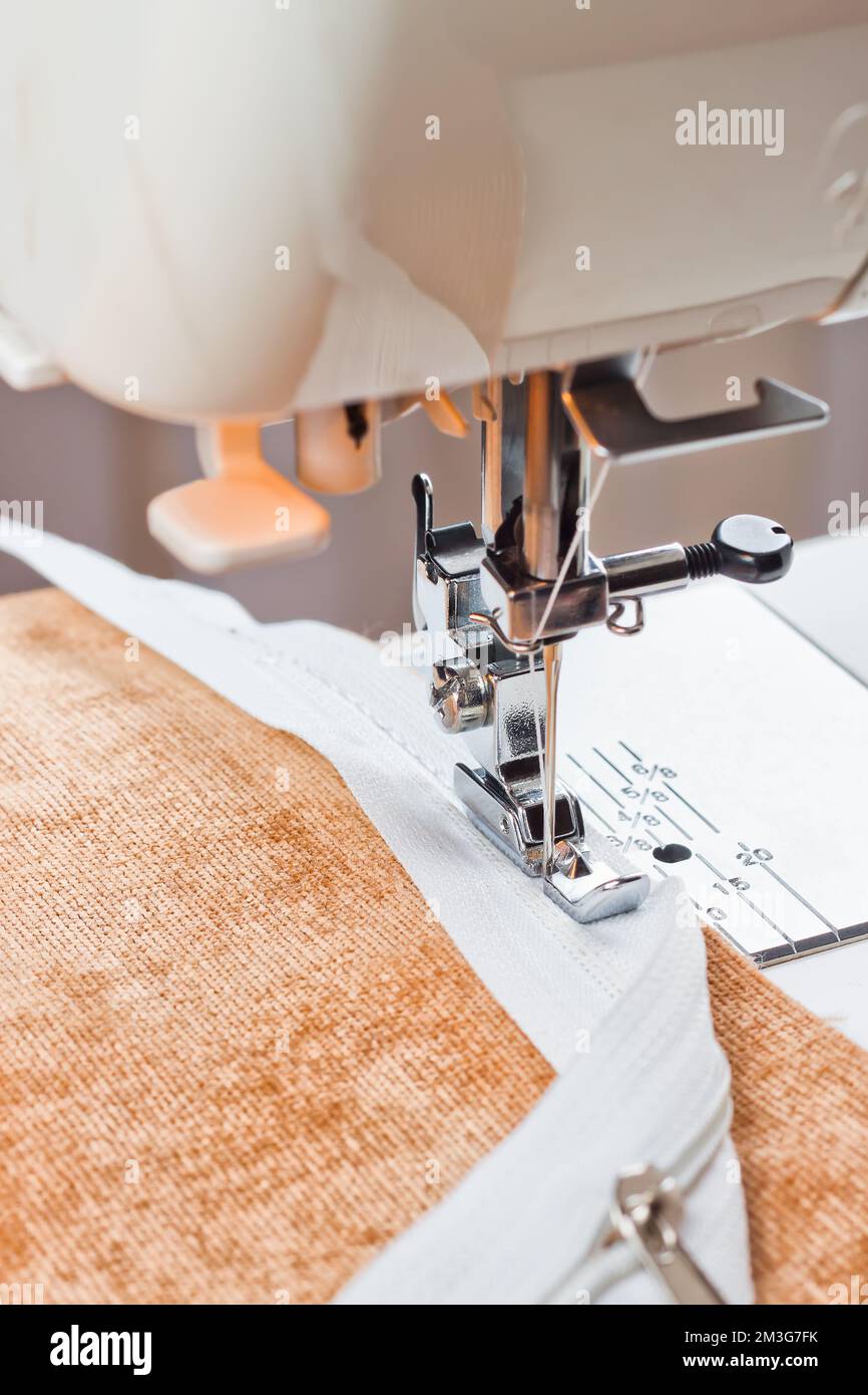 Modern sewing machine sews on the zipper on beige item of clothing ...