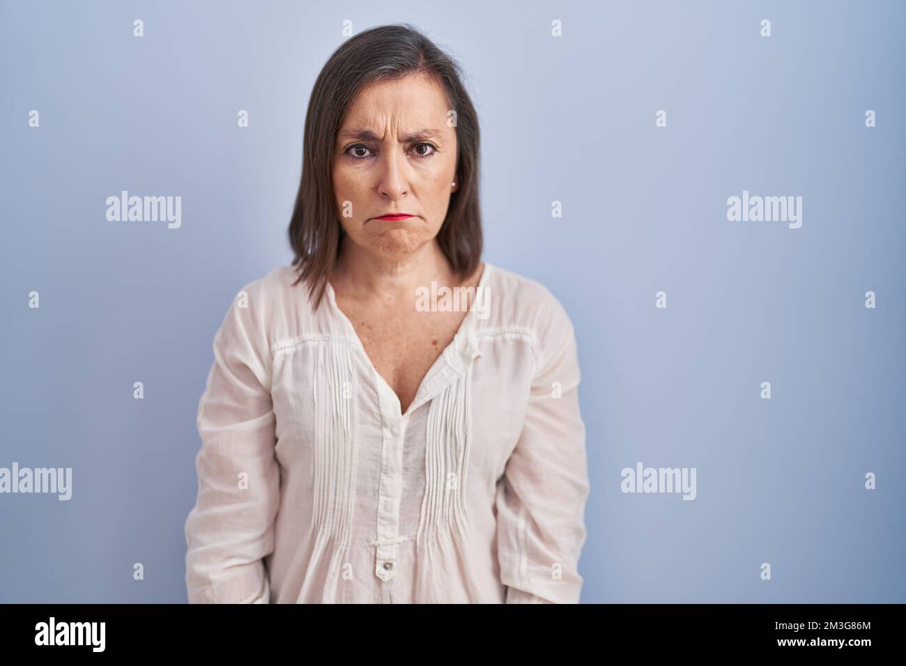 Middle age hispanic woman standing over blue background skeptic and ...
