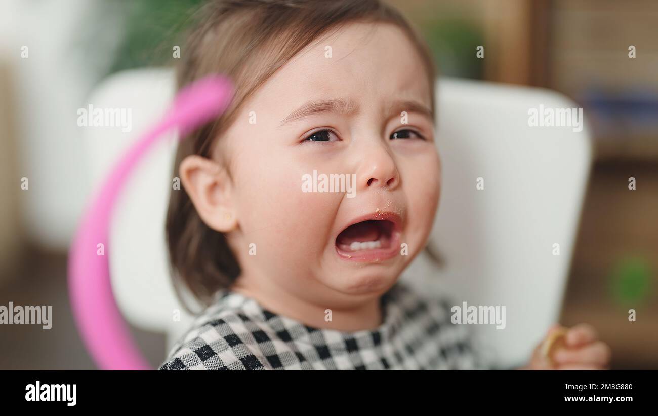 Adorable chinese girl sitting table holding toy crying at kindergarten ...