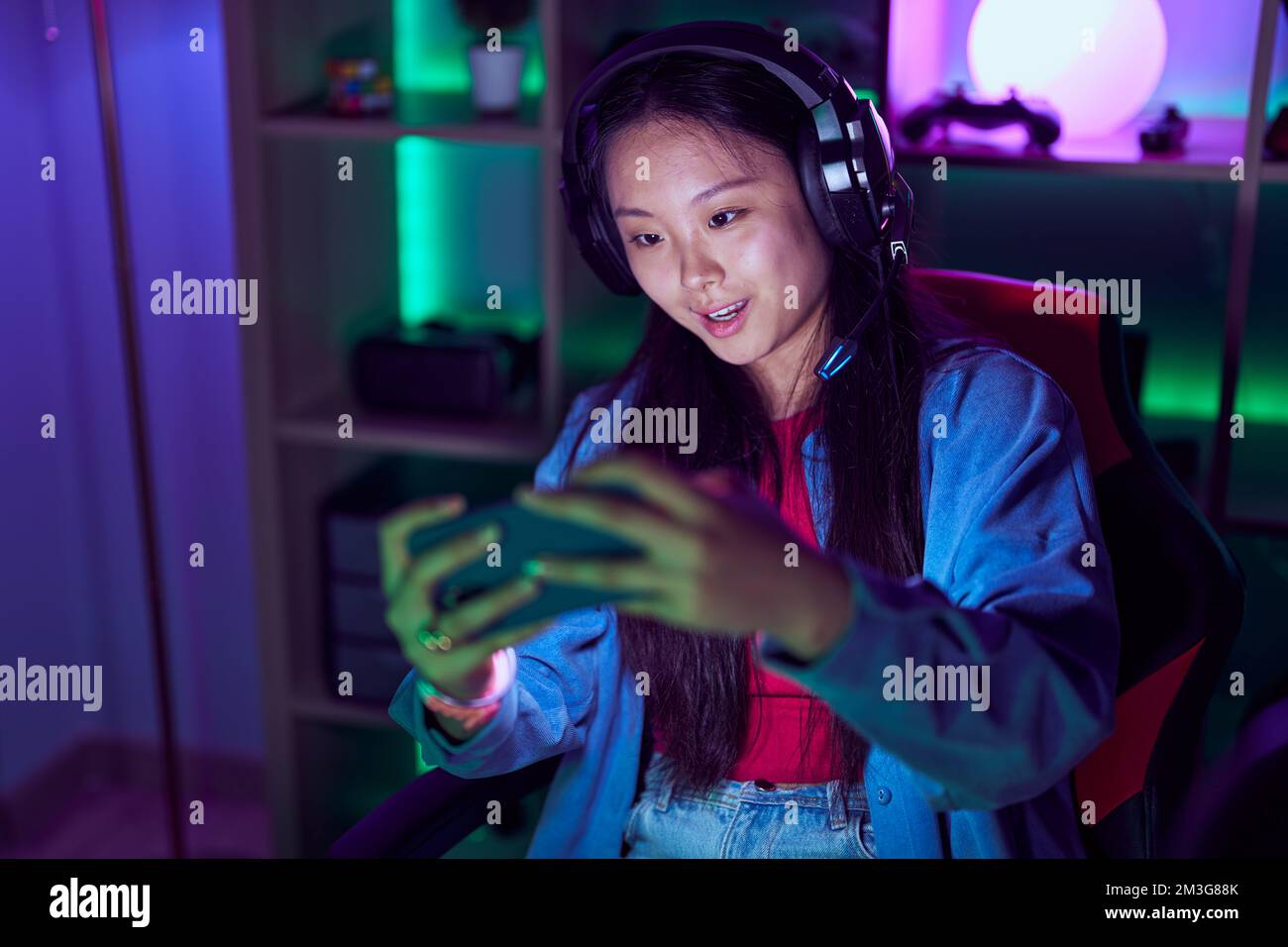 Young chinese woman streamer playing video game using smartphone at ...