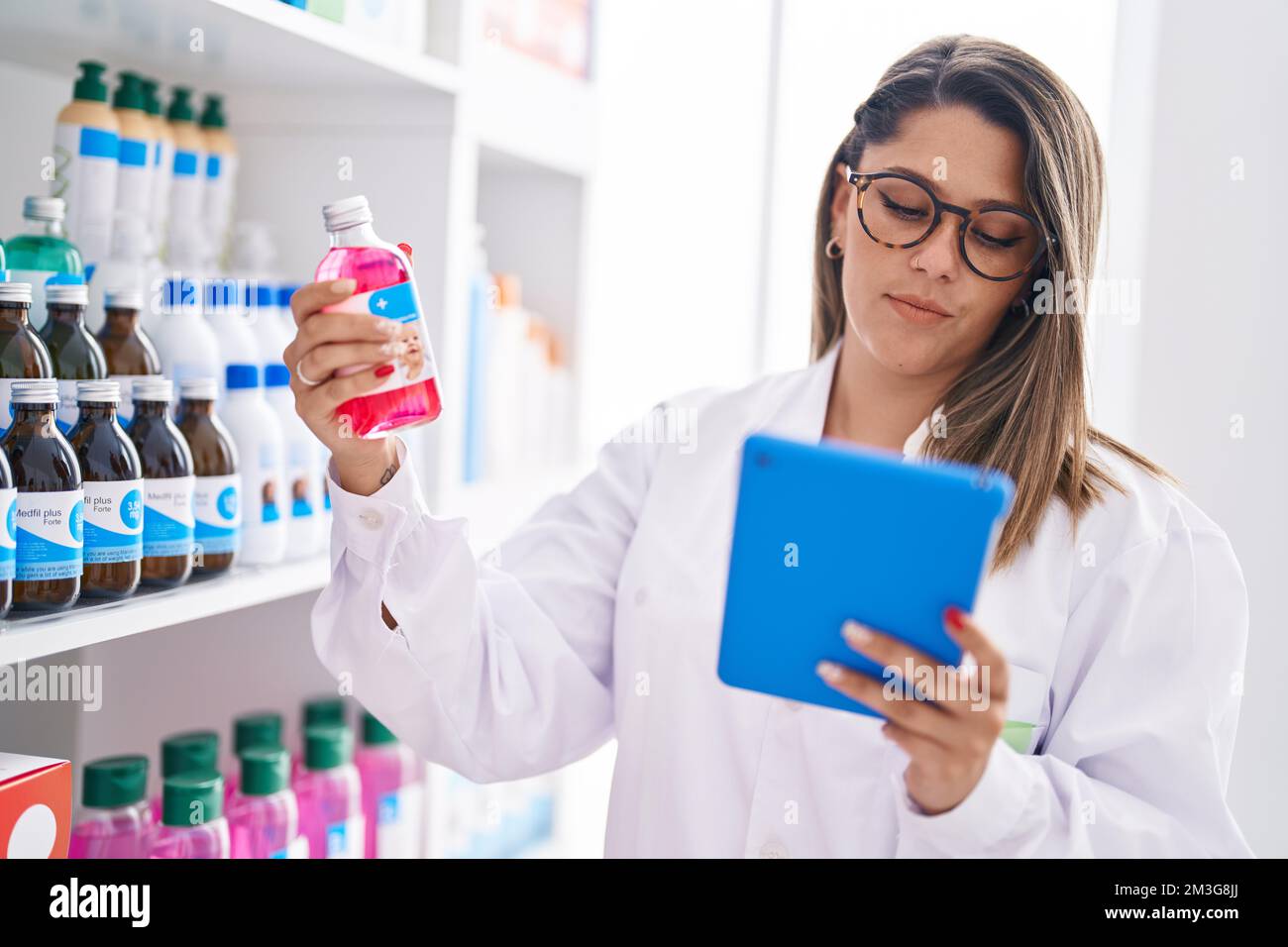 Young hispanic woman pharmacist using touchpad holding medicine bottle ...