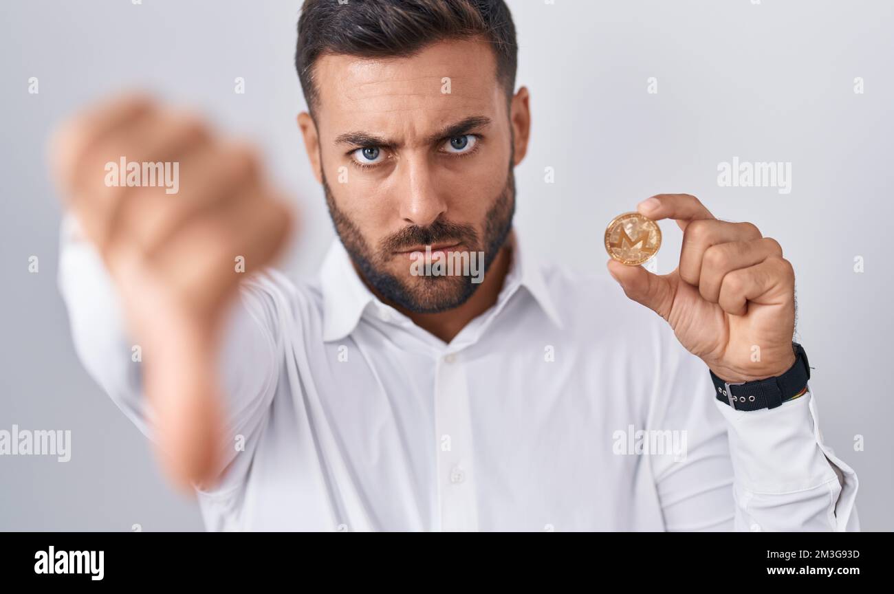 Handsome hispanic man holding monero cryptocurrency coin with angry ...