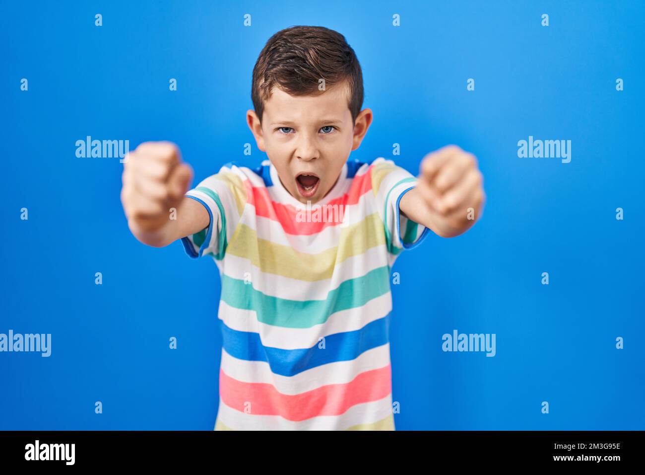 Young caucasian kid standing over blue background angry and mad raising ...