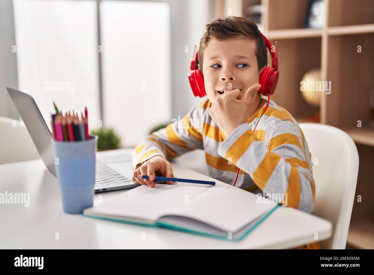 Young caucasian kid doing homework at home pointing thumb up to the ...