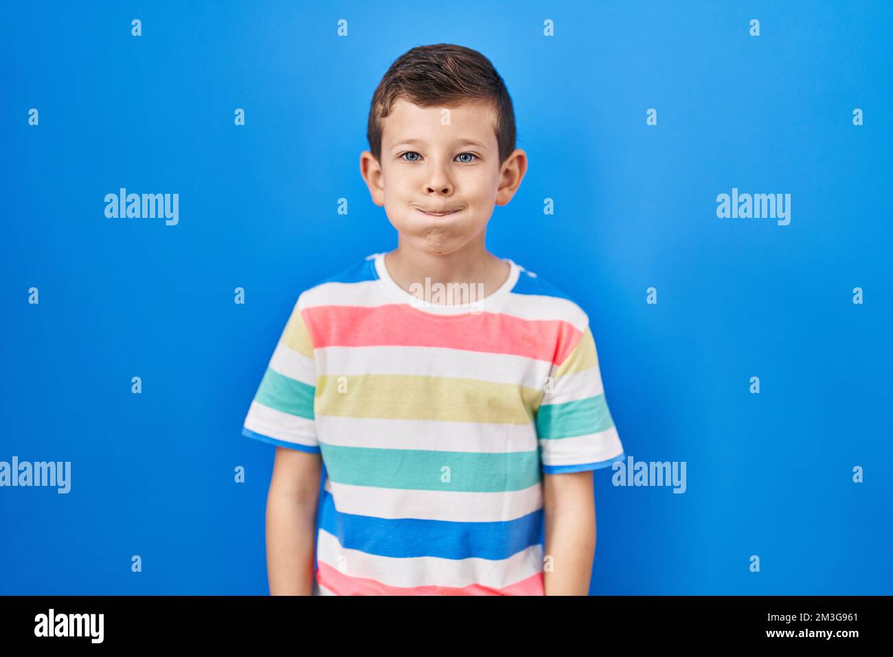 Young caucasian kid standing over blue background puffing cheeks with ...
