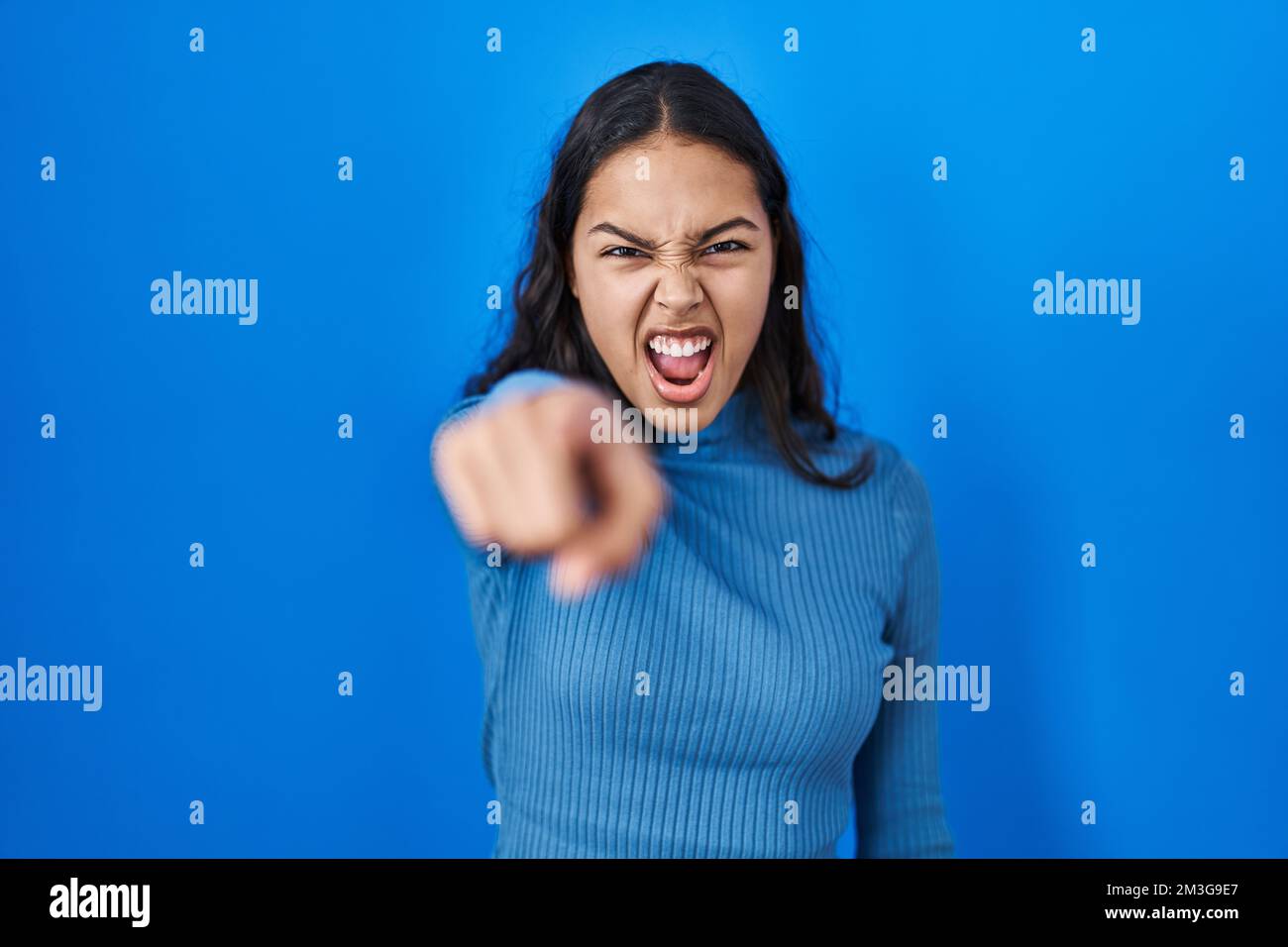 Young brazilian woman standing over blue isolated background pointing ...