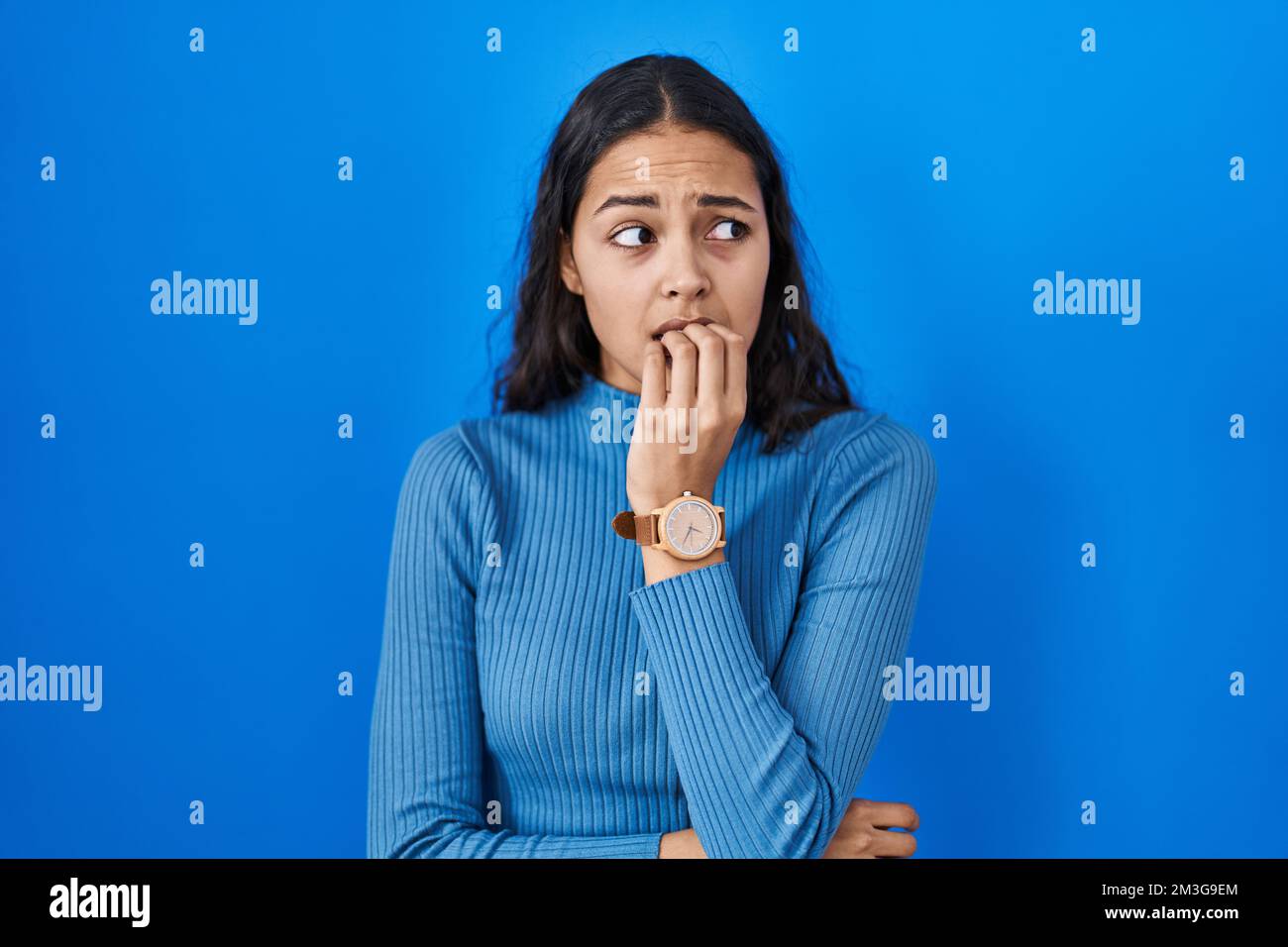 Young brazilian woman standing over blue isolated background looking ...