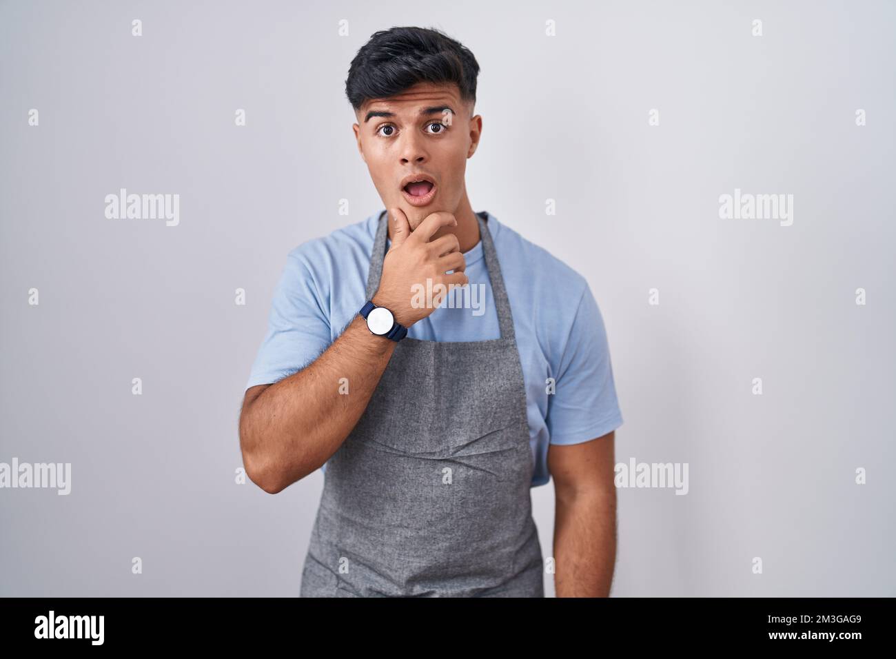 Hispanic young man wearing apron over white background looking ...