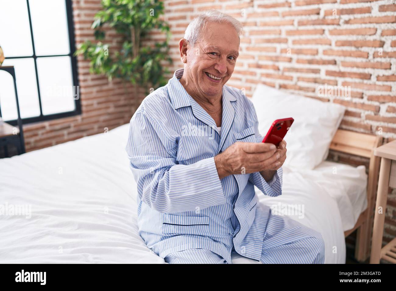 Middle age grey-haired man using smartphone sitting on bed at bedroom ...