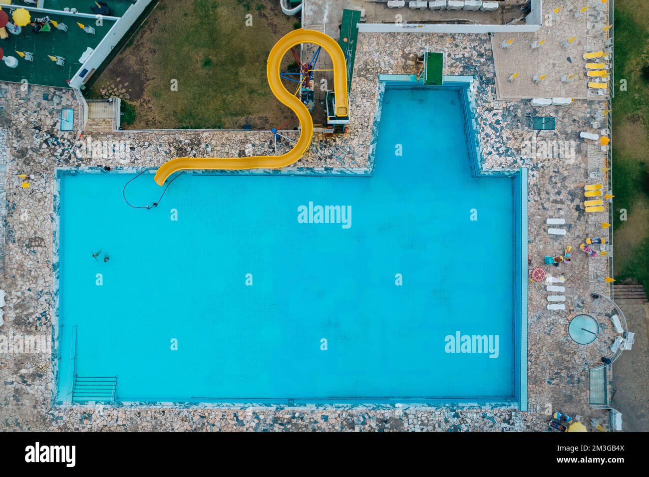 A top-down drone shot of an outdoor swimming pool with a big yellow ...