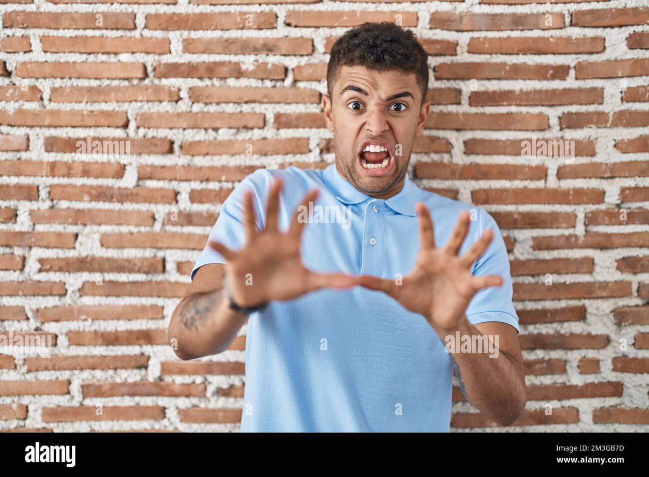Brazilian young man standing over brick wall afraid and terrified with ...