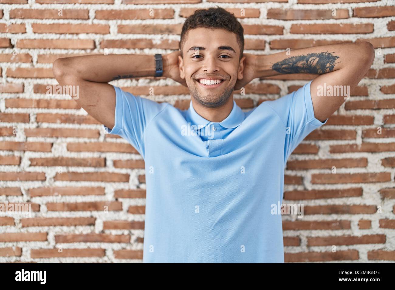 Brazilian young man standing over brick wall relaxing and stretching ...