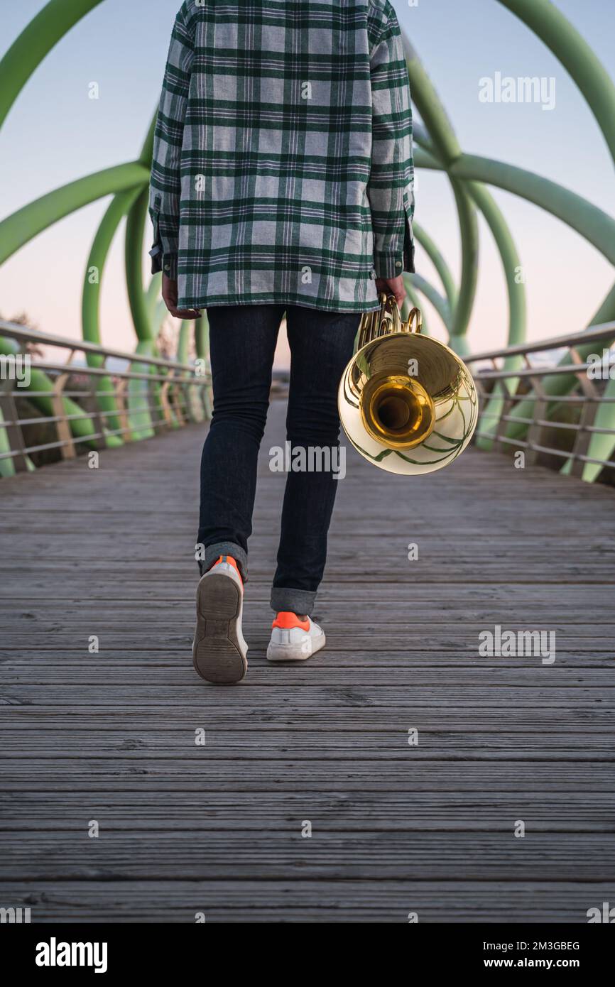 Musician walking on a bridge with his horn in his hand Stock Photo - Alamy