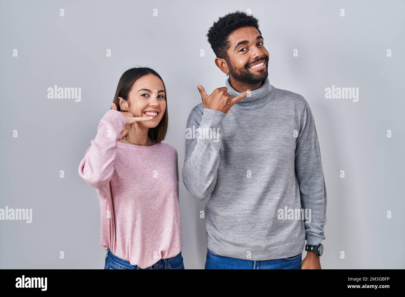 Young hispanic couple standing together smiling doing phone gesture ...