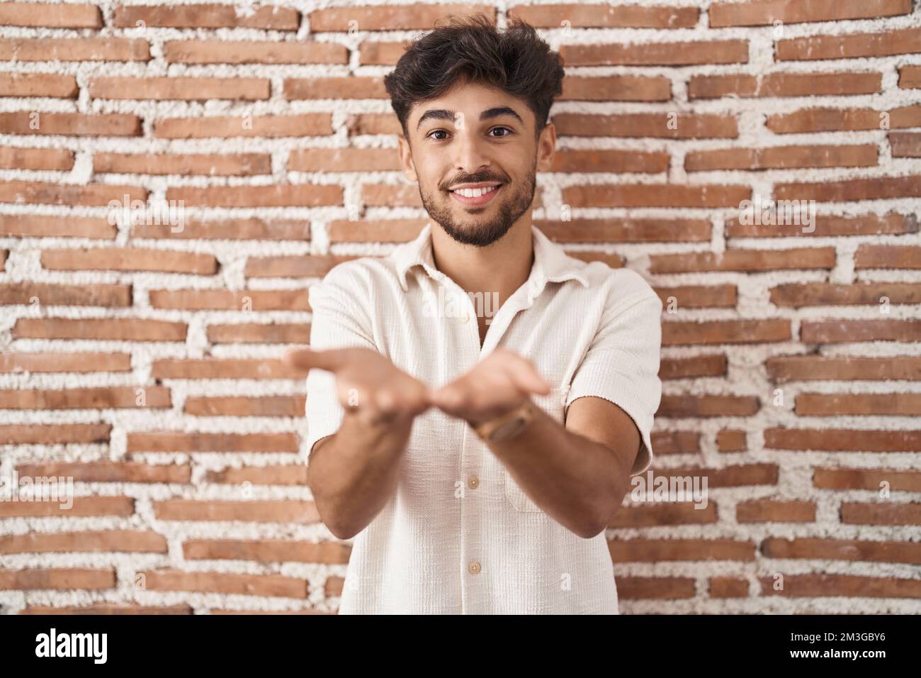 Arab man with beard standing over bricks wall background smiling with ...