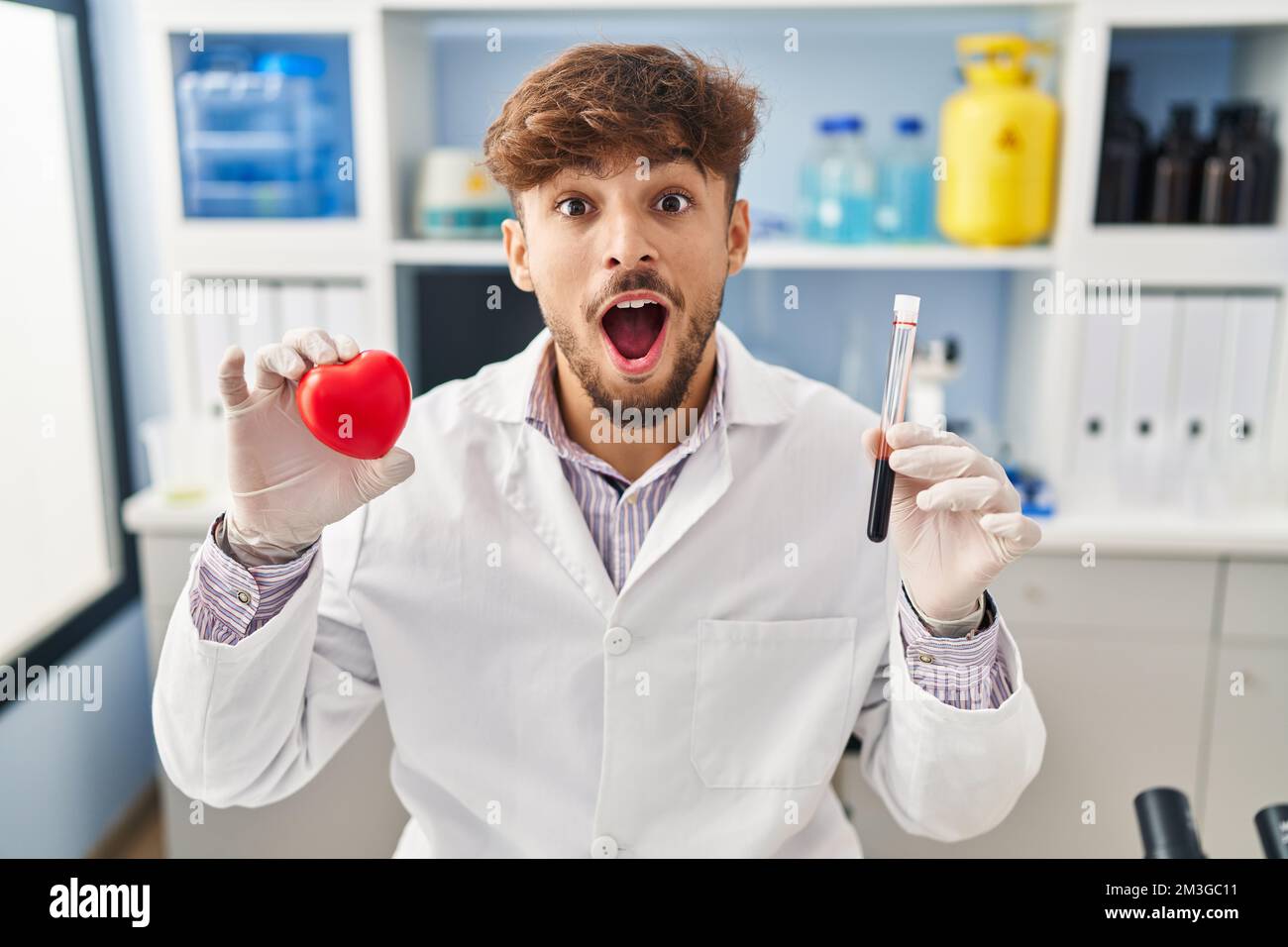 Arab man with beard working at scientist laboratory holding blood samples celebrating crazy and ...