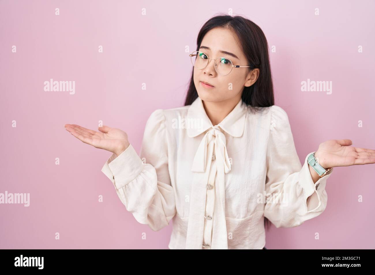 Young chinese woman standing over pink background clueless and confused ...