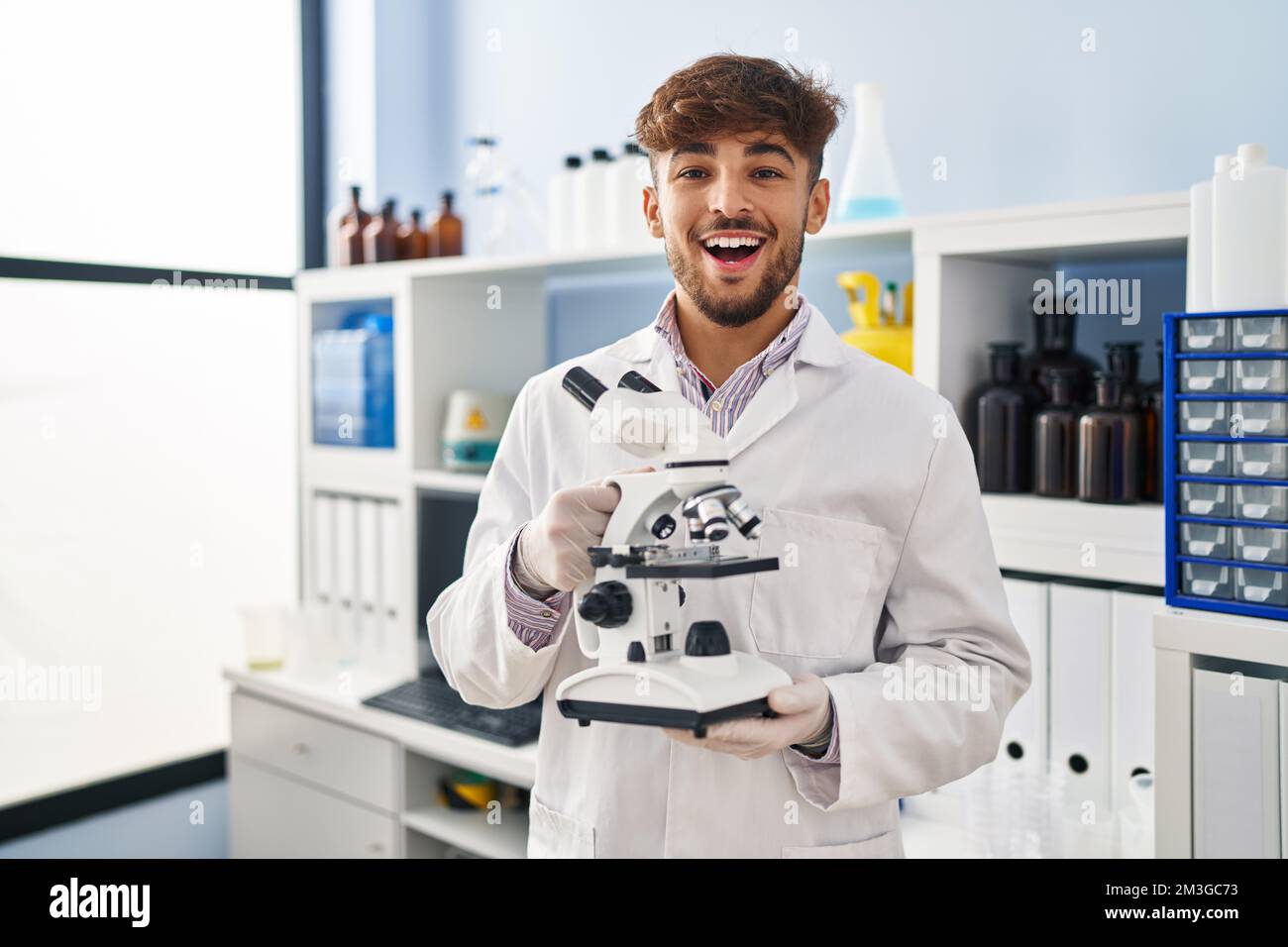 Arab man with beard working at scientist laboratory holding microscope ...