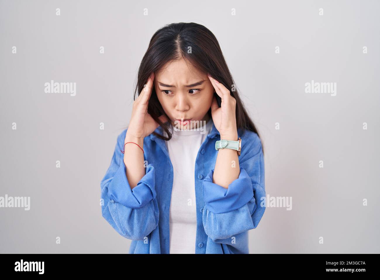 Young chinese woman standing over white background with hand on head ...