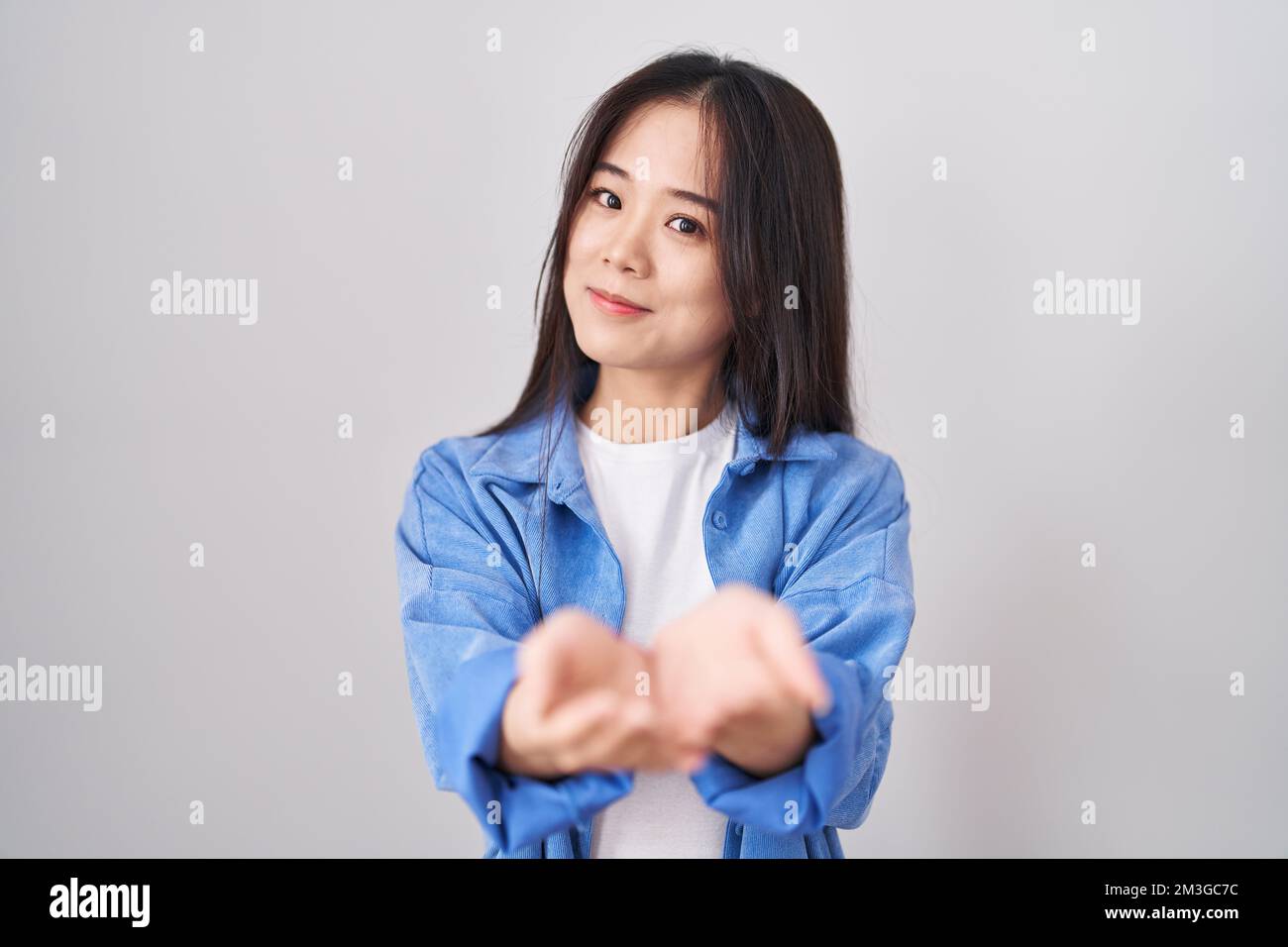 Young chinese woman standing over white background smiling with hands ...