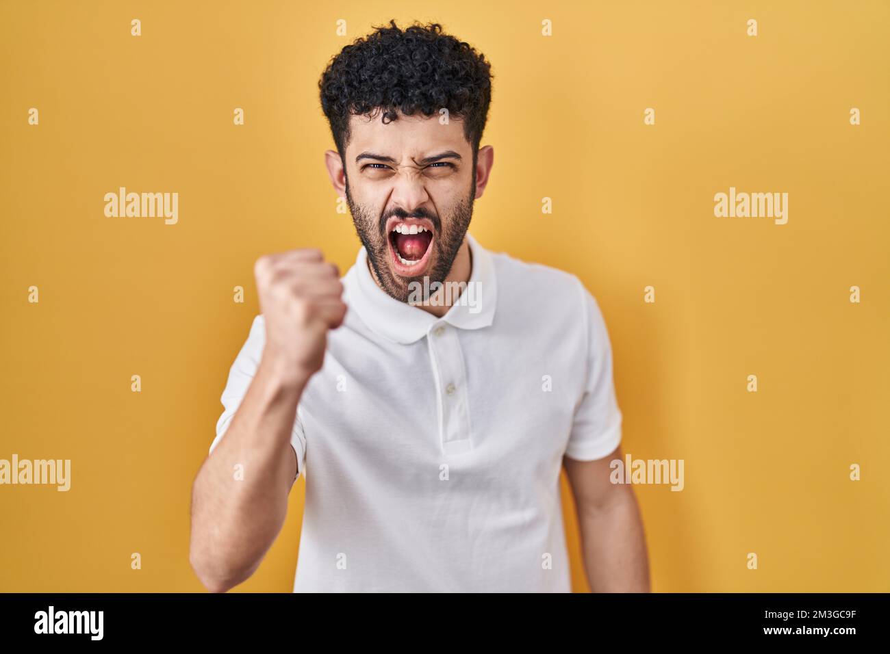 Arab man standing over yellow background angry and mad raising fist ...