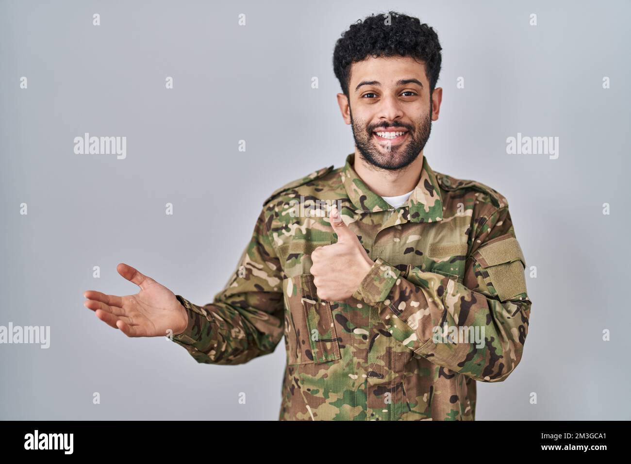 Arab man wearing camouflage army uniform showing palm hand and doing ok ...