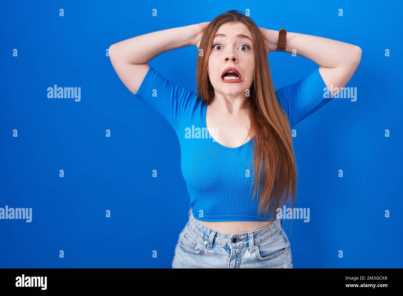 Redhead Woman Standing Over Blue Background Crazy And Scared With Hands