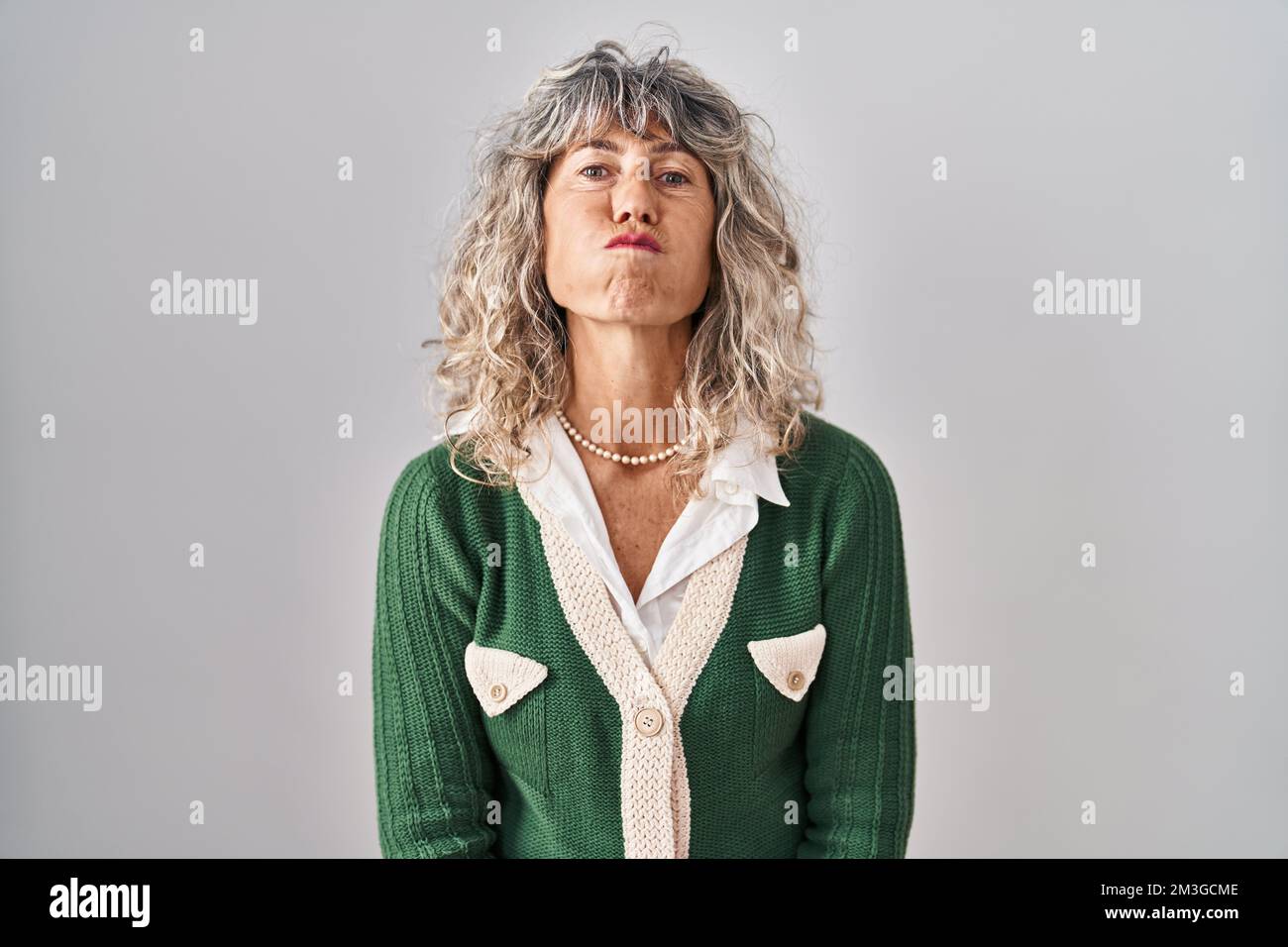 Middle age woman standing over white background puffing cheeks with ...
