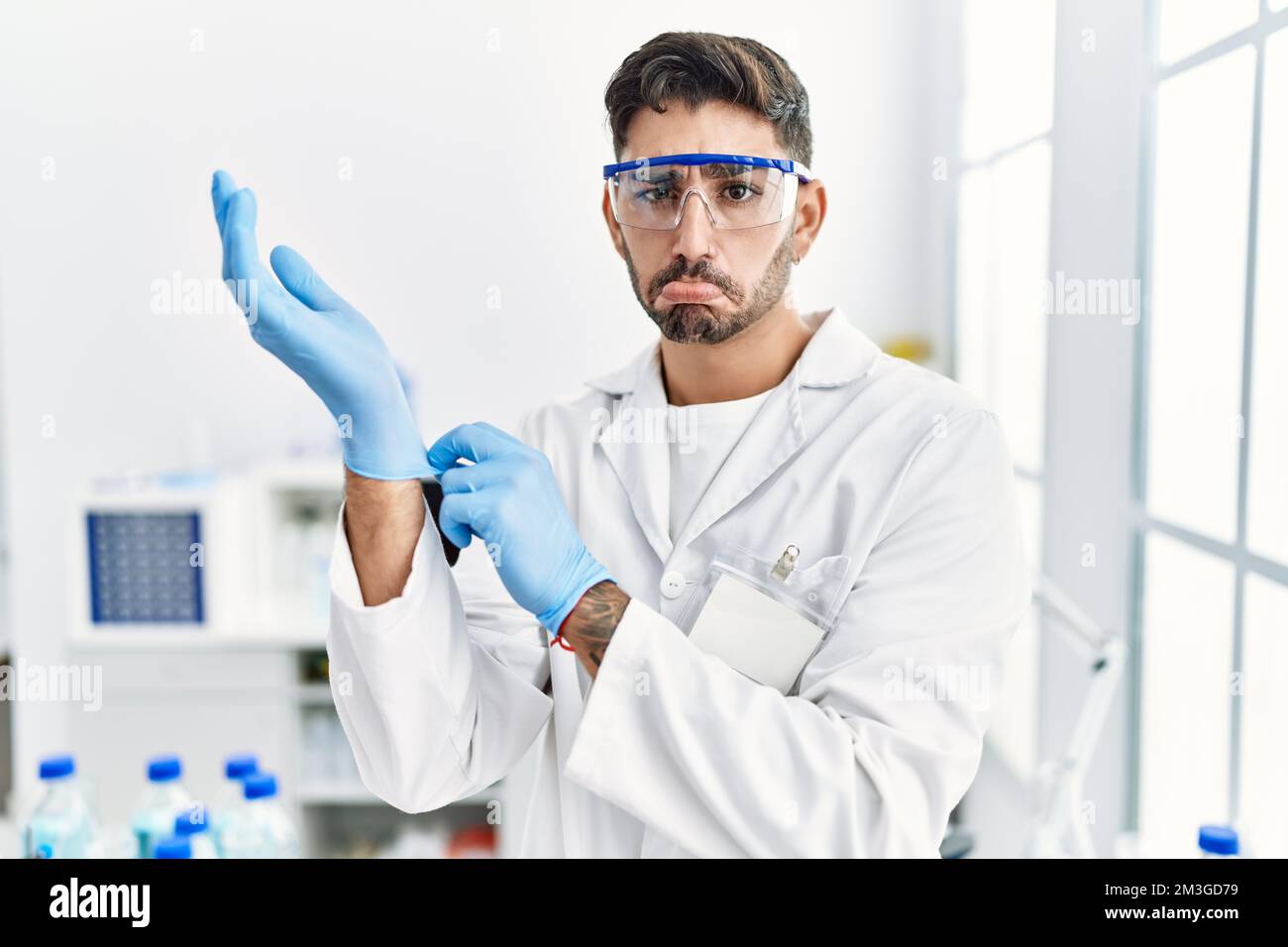 Young hispanic man working at scientist laboratory putting gloves on ...