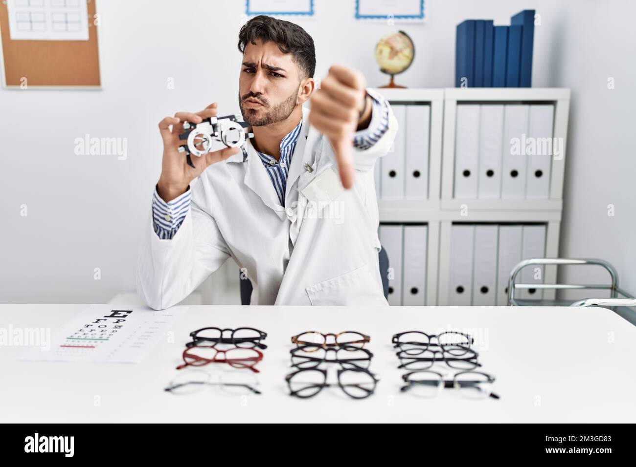 Young optician man holding optometry glasses looking unhappy and angry ...