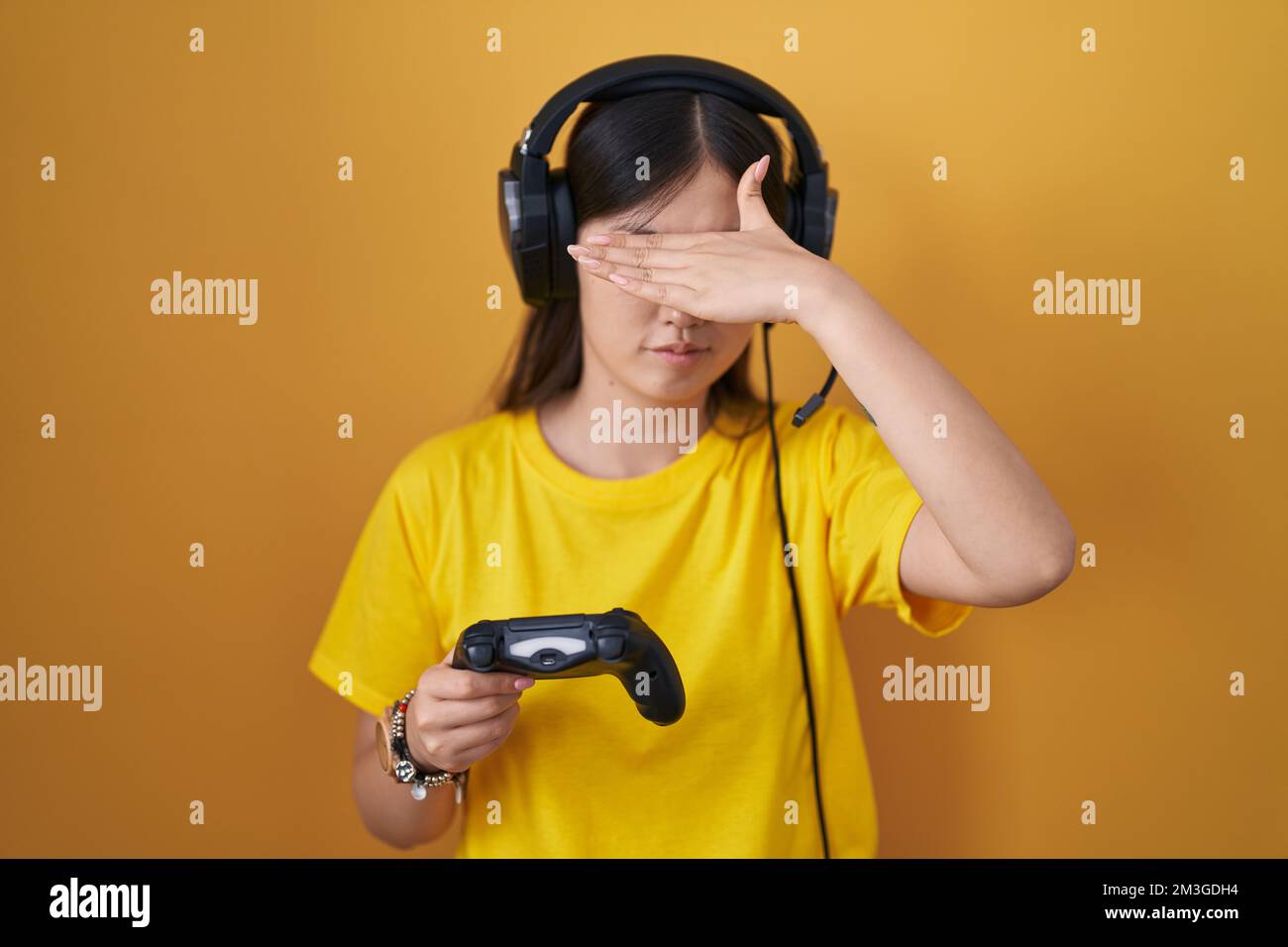 Chinese young woman playing video game holding controller covering eyes ...