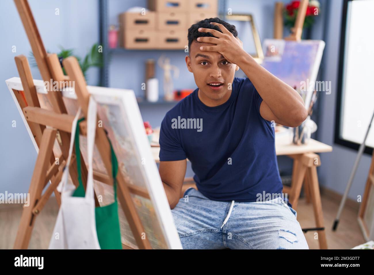 Young hispanic man painting sitting at art studio stressed and ...