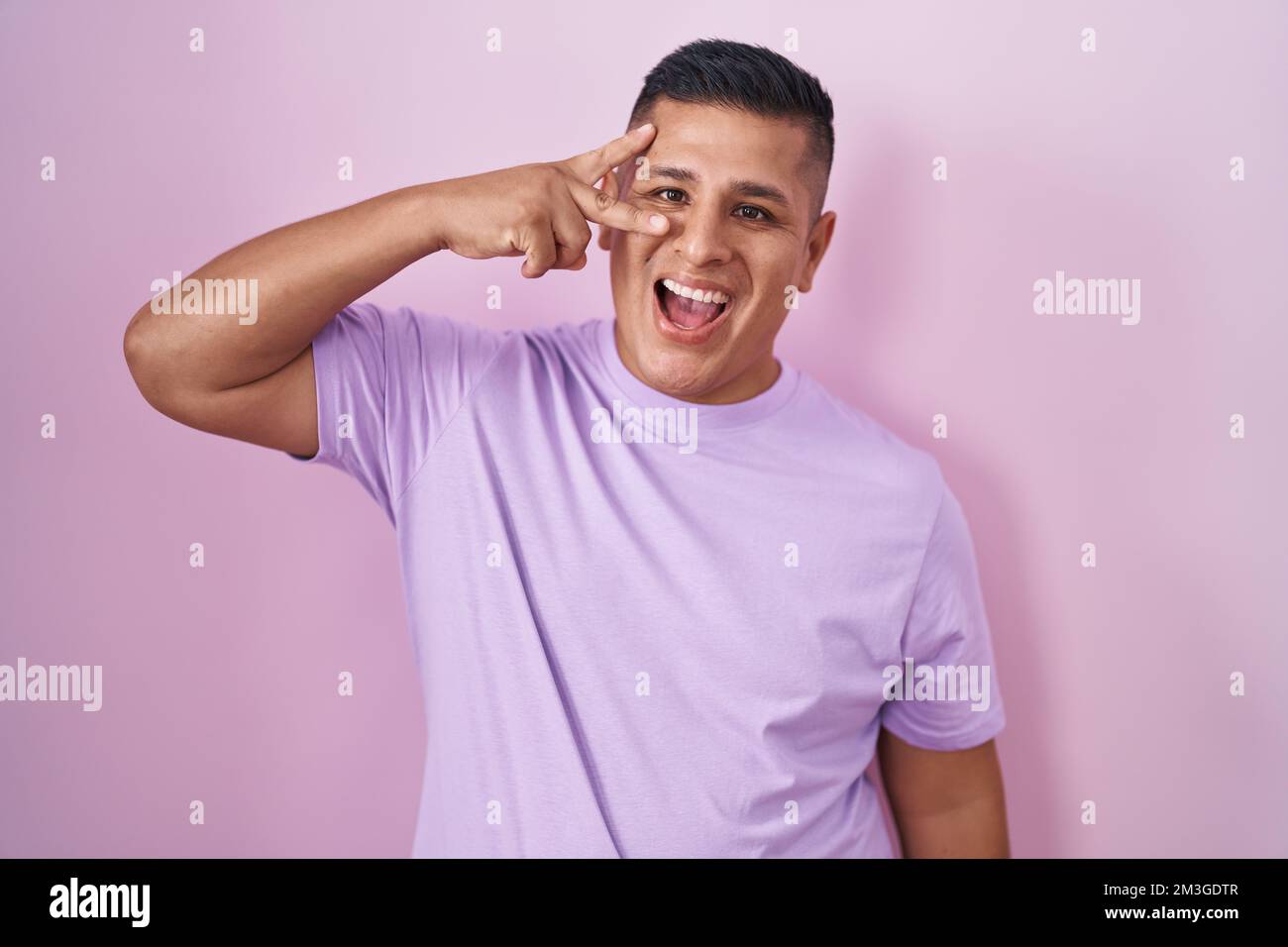 Young hispanic man standing over pink background doing peace symbol ...