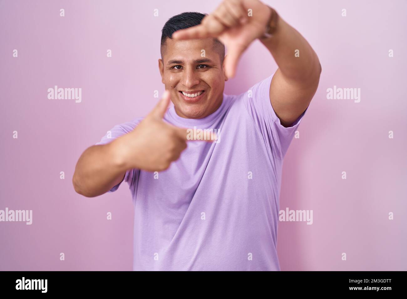 Young hispanic man standing over pink background smiling making frame ...