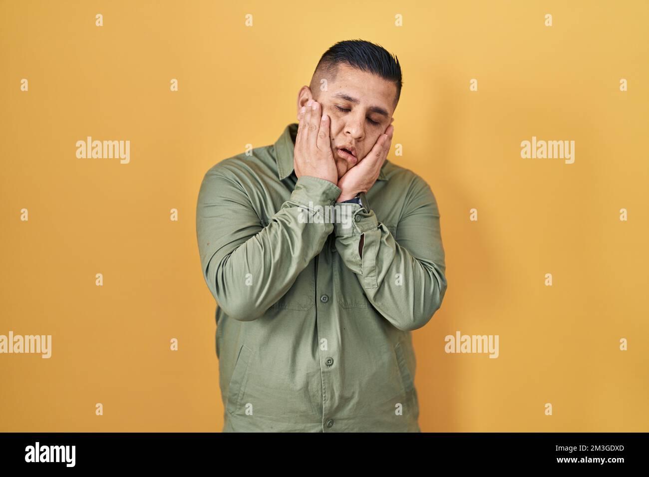 Hispanic young man standing over yellow background tired hands covering ...