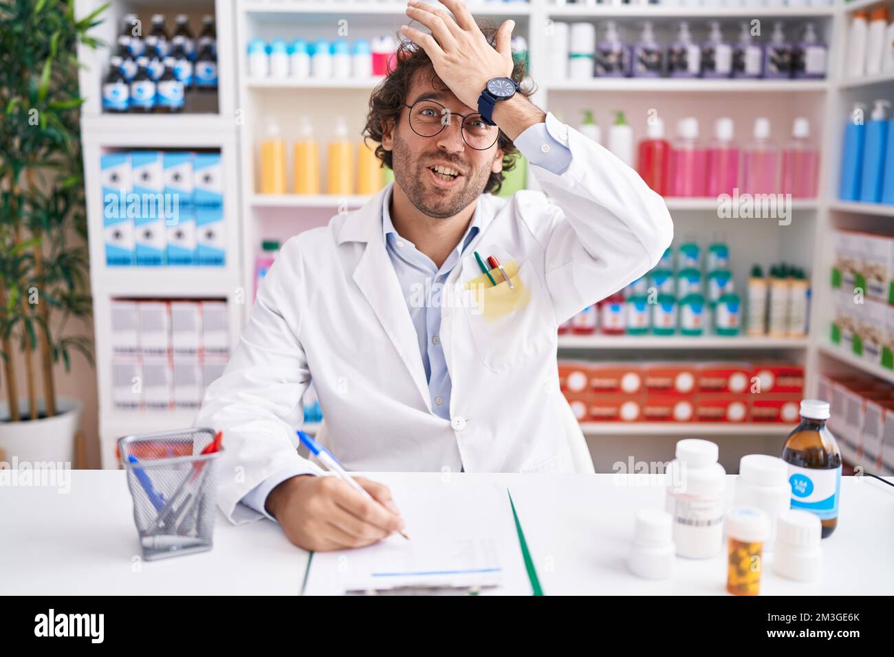 Hispanic young man working at pharmacy drugstore surprised with hand on ...