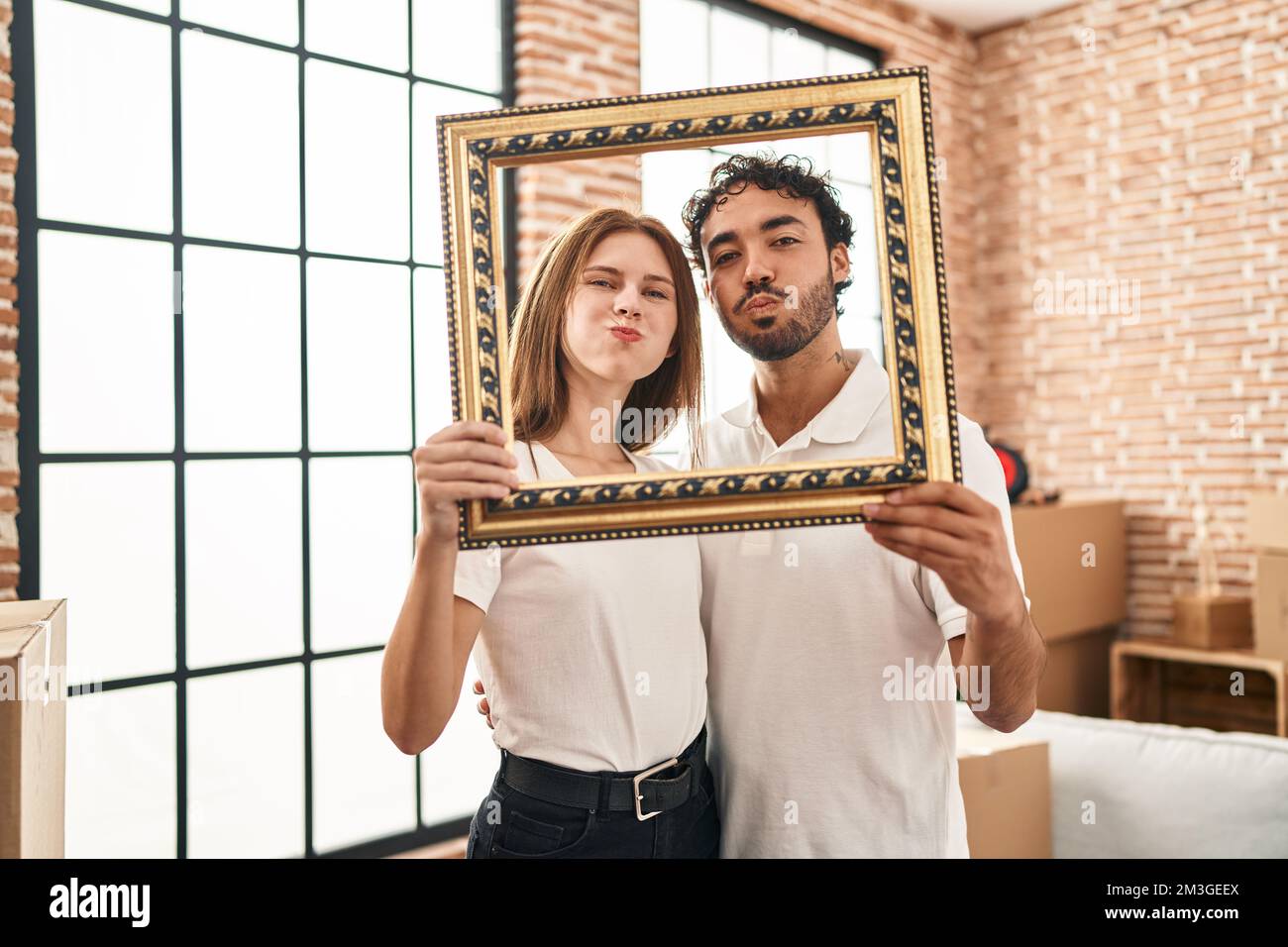 Young two people holding empty frame together puffing cheeks with funny ...