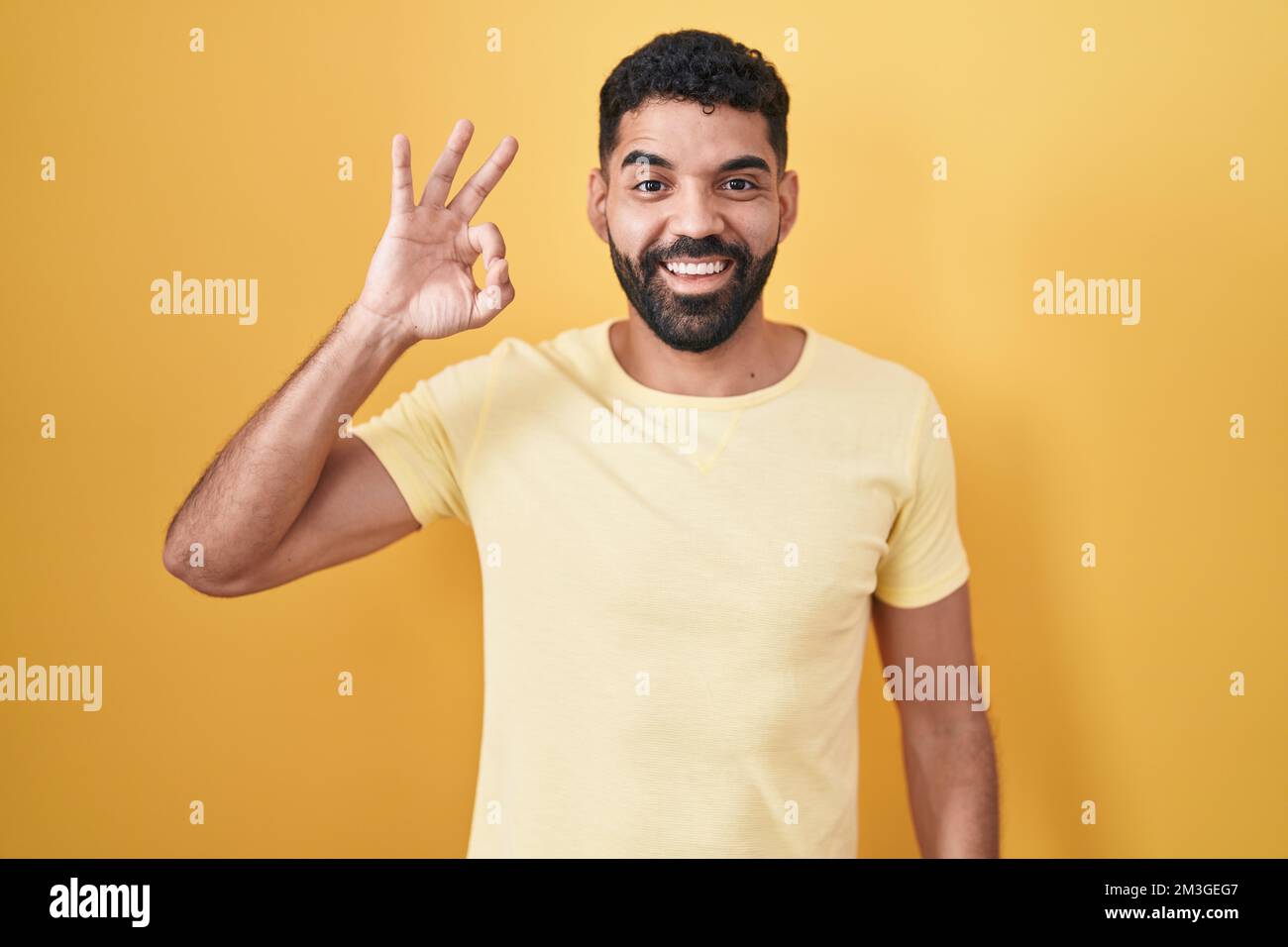 Hispanic man with beard standing over yellow background smiling ...