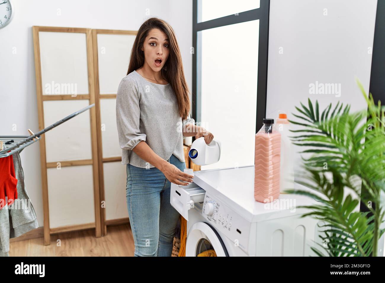 Young brunette woman putting detergent in washing machine afraid and ...