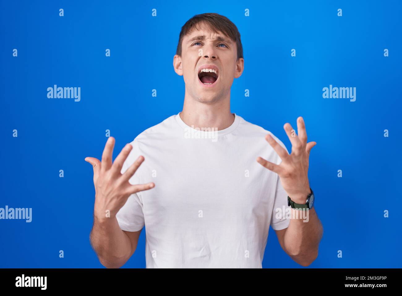 Caucasian blond man standing over blue background crazy and mad ...