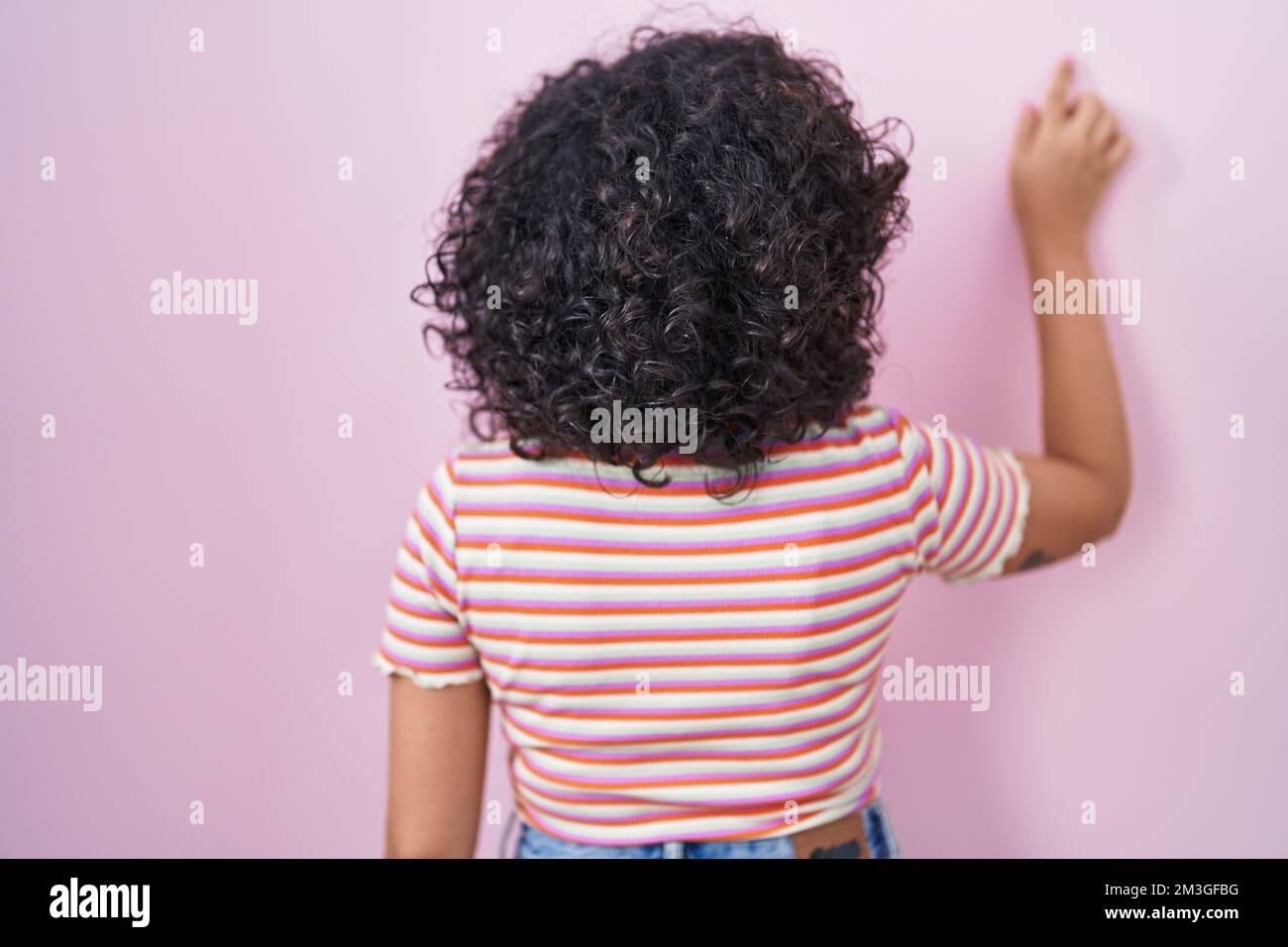 Young middle east woman standing over pink background posing backwards ...