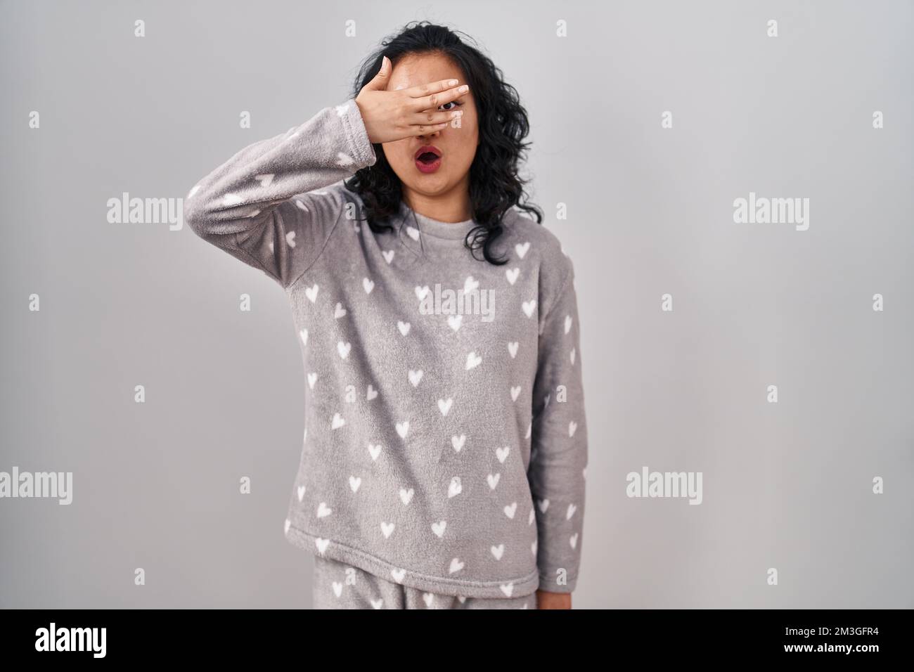 Young asian woman wearing pajama peeking in shock covering face and ...