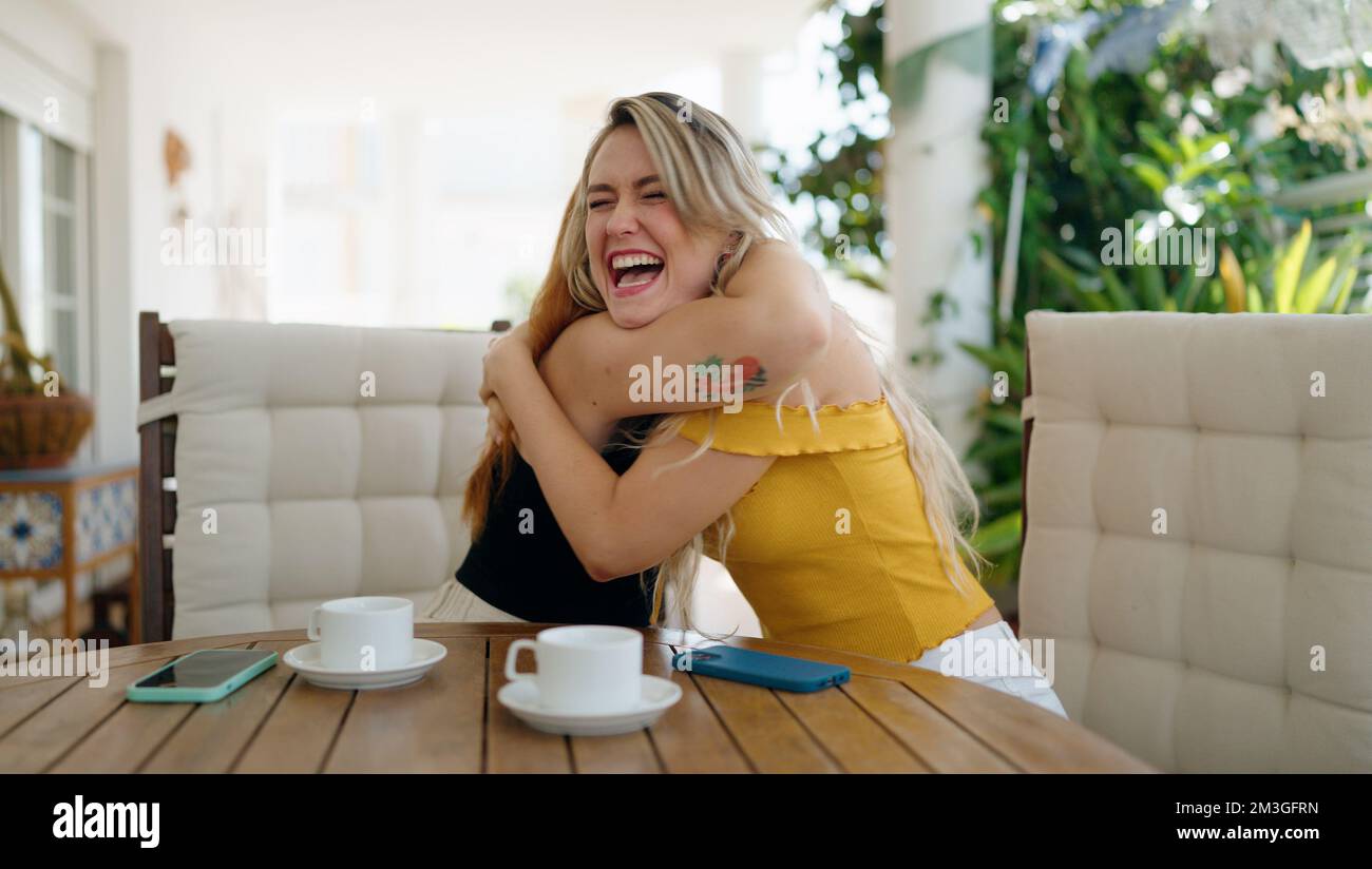 Two women sitting on table hugging each other at home terrace Stock ...