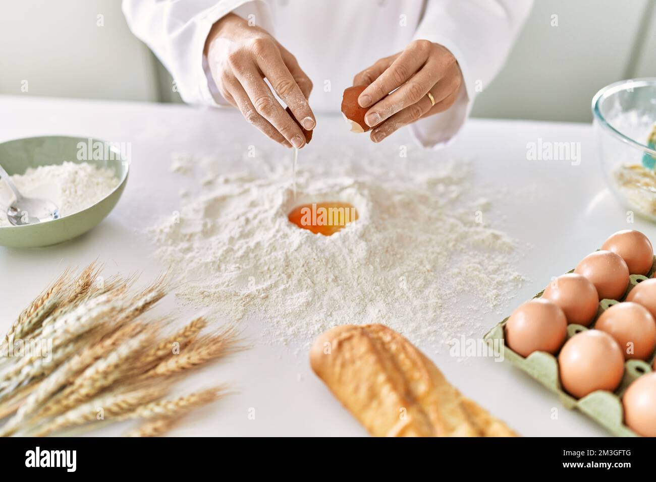 Young woman wearing cook uniform cracking egg on flour at kitchen Stock ...