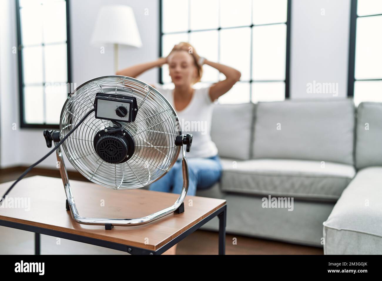Young blonde woman using fan at home Stock Photo - Alamy